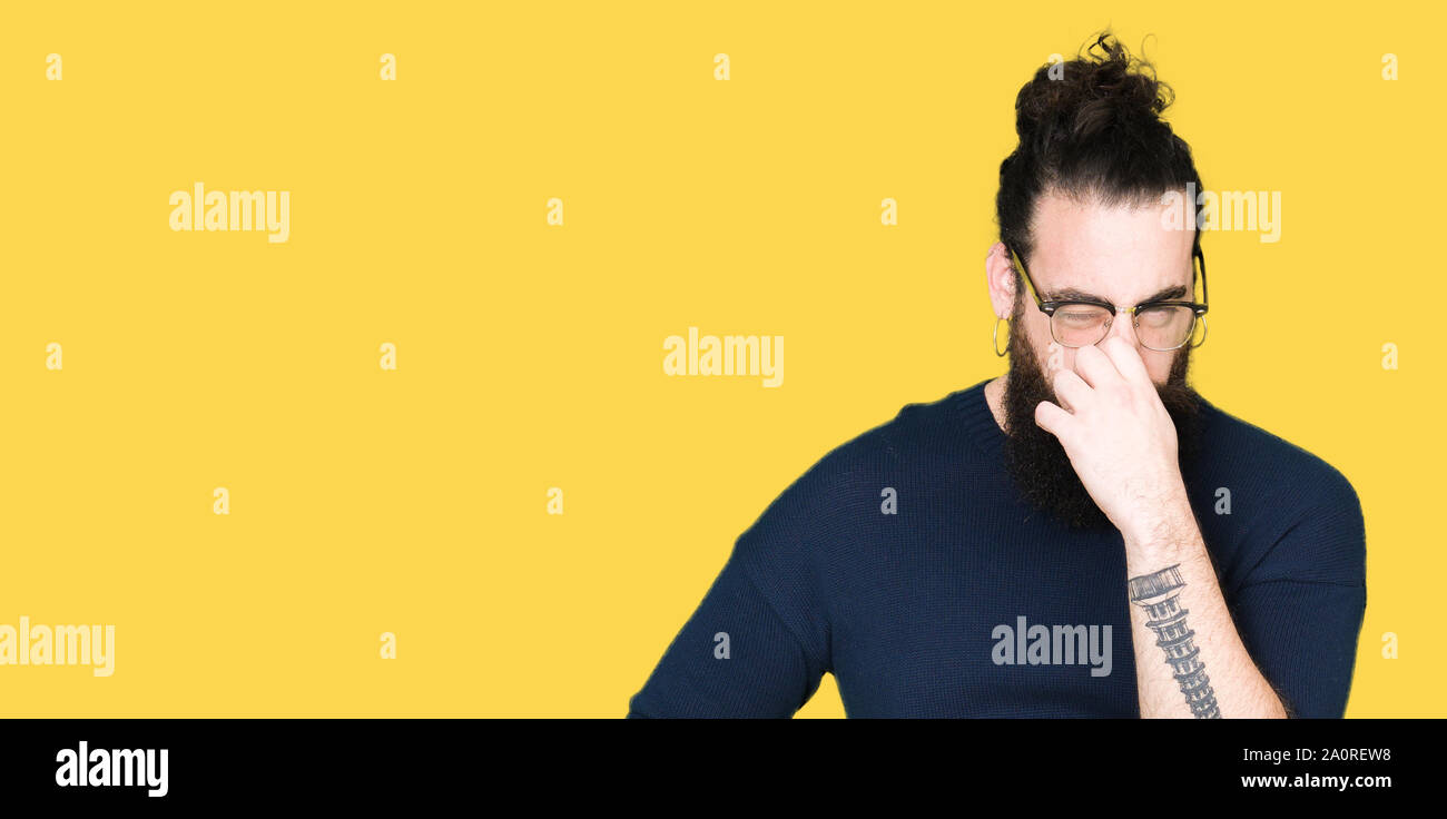 Young hipster man with long hair and beard wearing glasses smelling ...