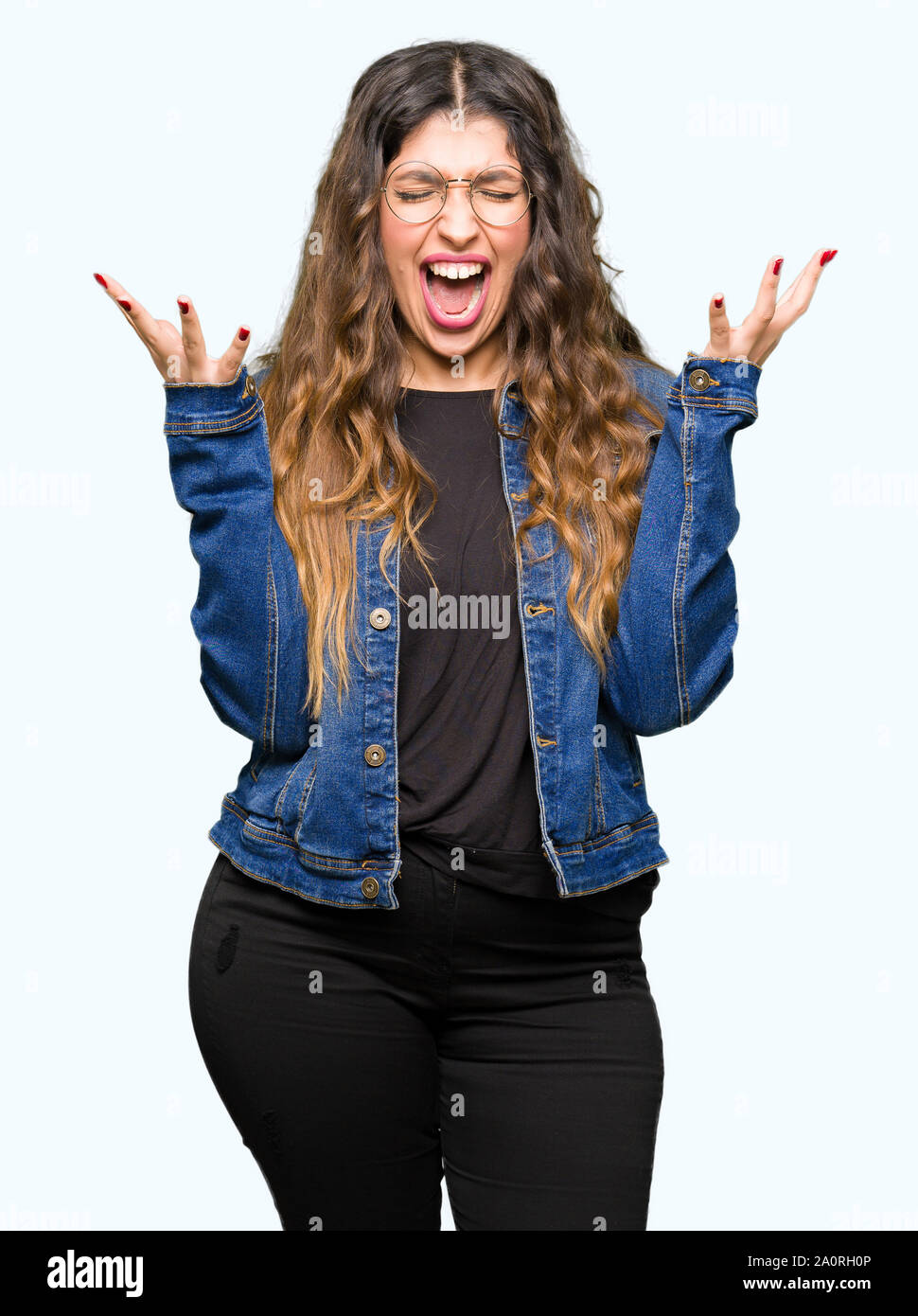 Young beautiful woman wearing glasses and denim jacket celebrating mad ...
