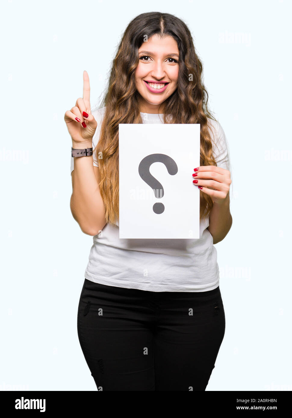 Young adult woman holding paper with question mark surprised with an ...