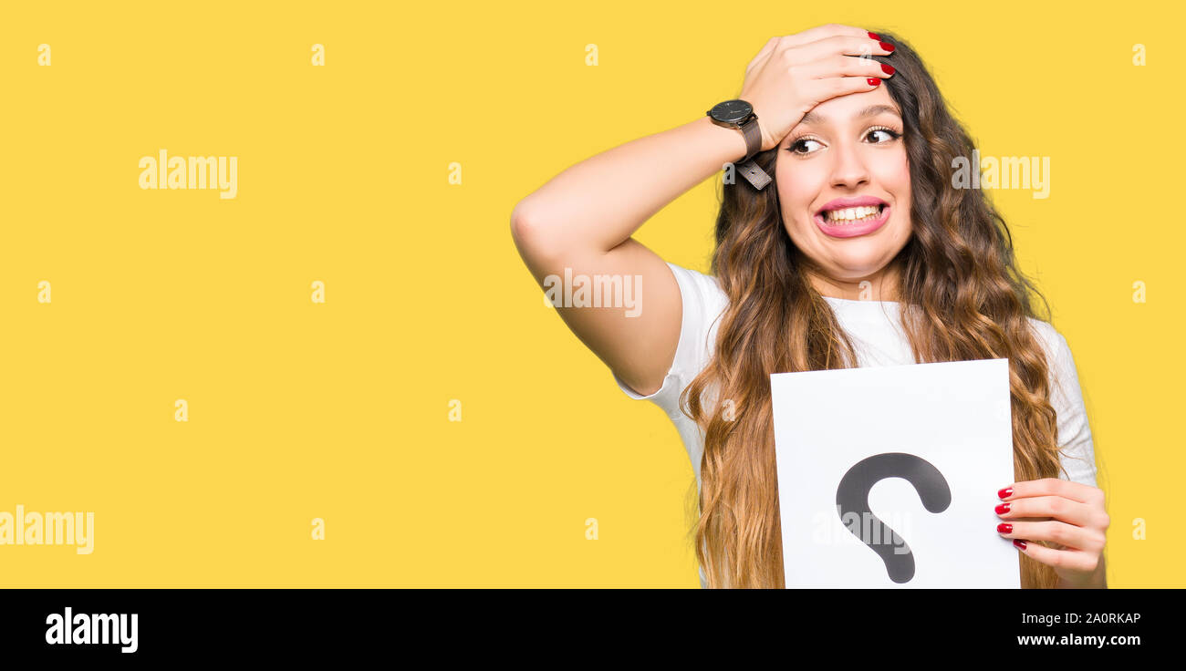 Young adult woman holding paper with question mark stressed with hand ...