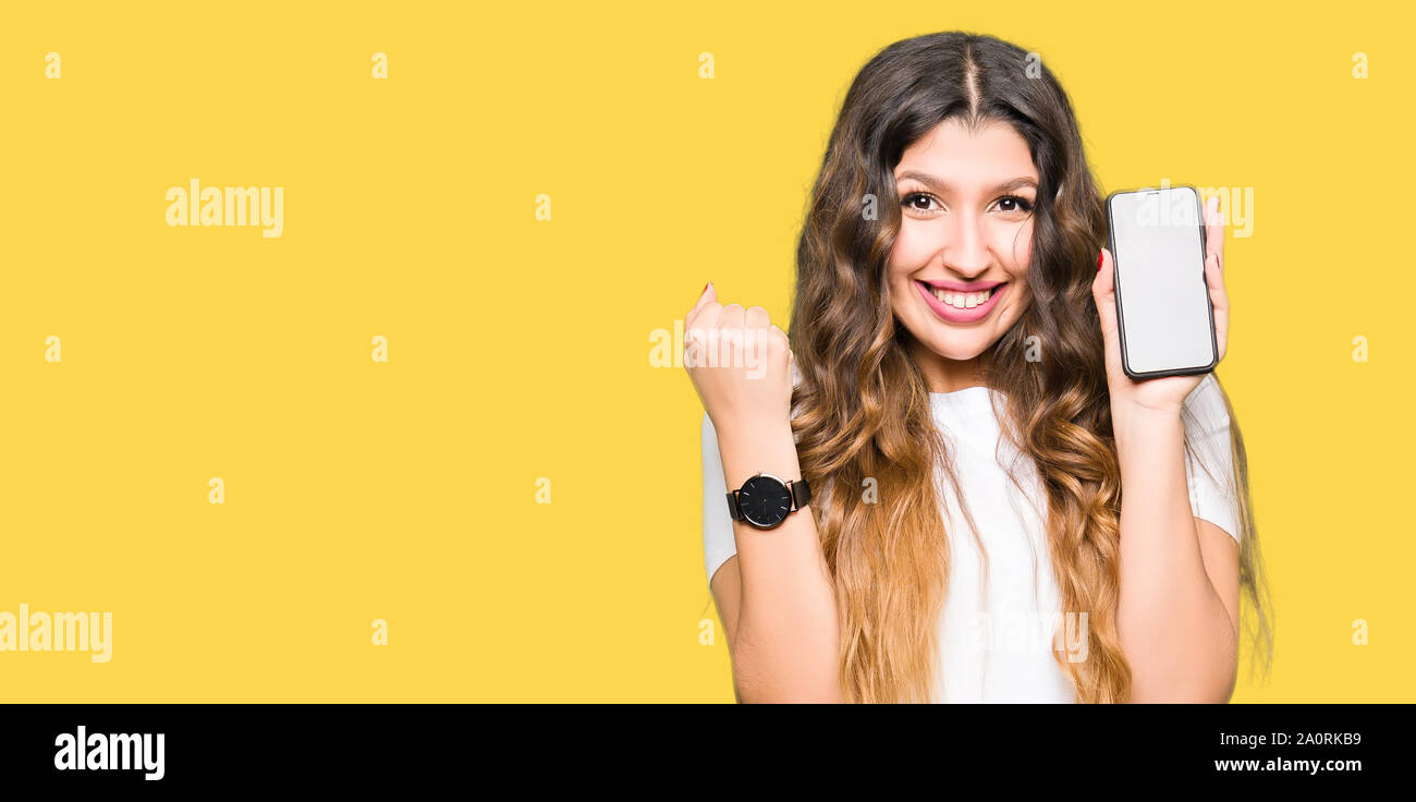 Young adult woman showing smartphone screen screaming proud and ...
