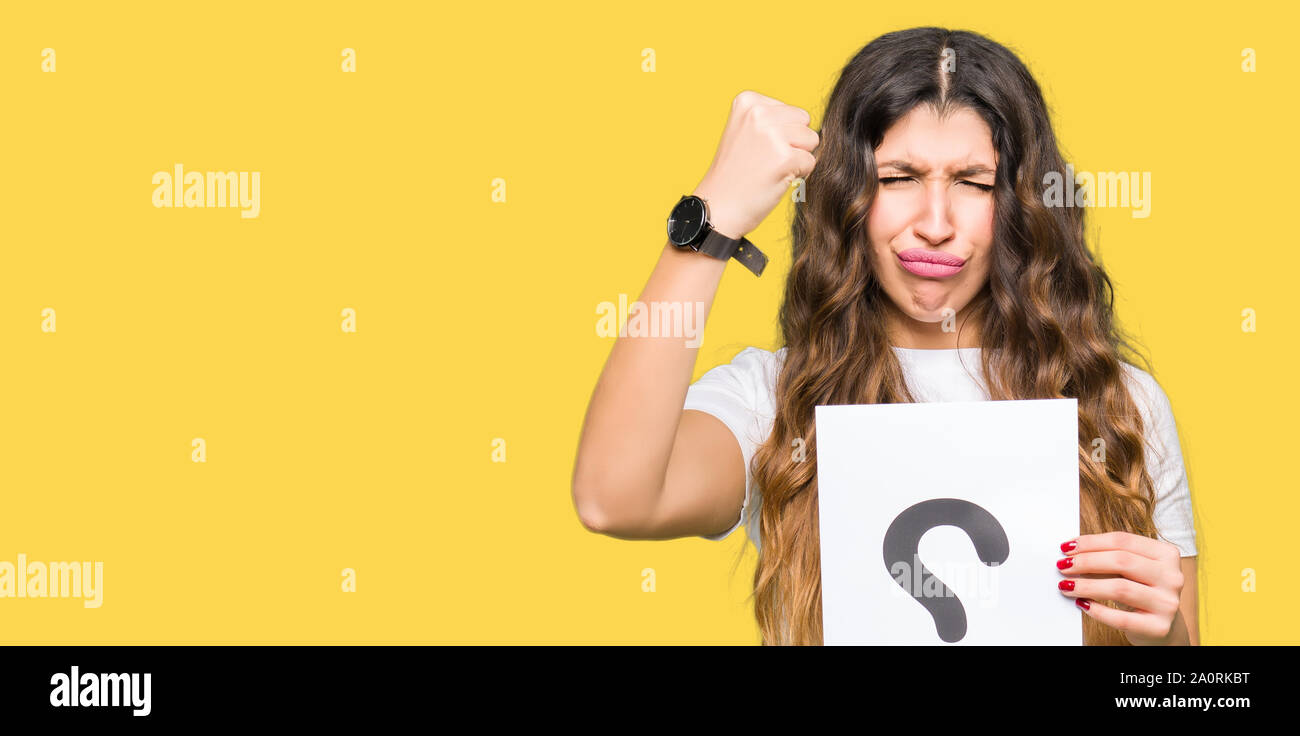 Young adult woman holding paper with question mark annoyed and ...