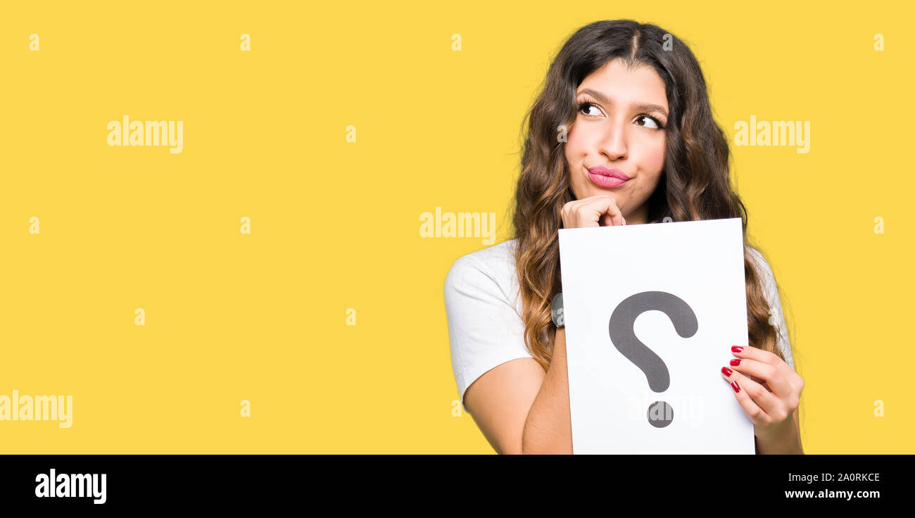 Young adult woman holding paper with question mark serious face ...