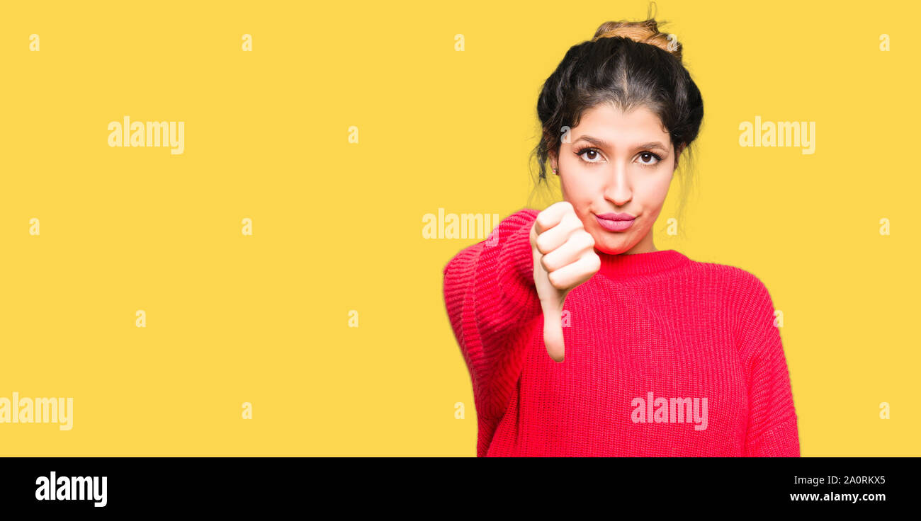 Young beautiful woman wearing red sweater and bun looking unhappy and ...