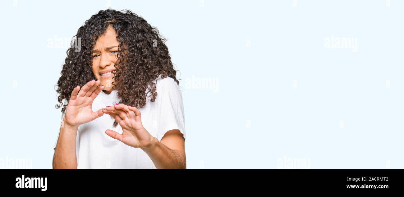 Young beautiful woman with curly hair wearing white t-shirt disgusted ...