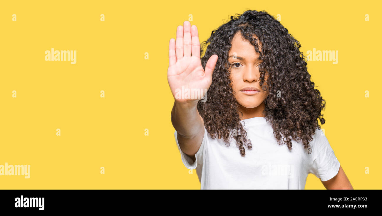 Young beautiful woman with curly hair wearing white t-shirt doing stop ...