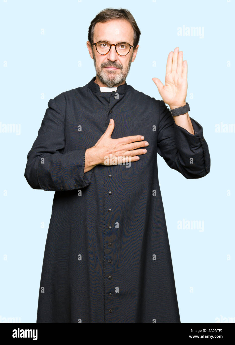 Middle age priest man wearing catholic robe Swearing with hand on chest ...