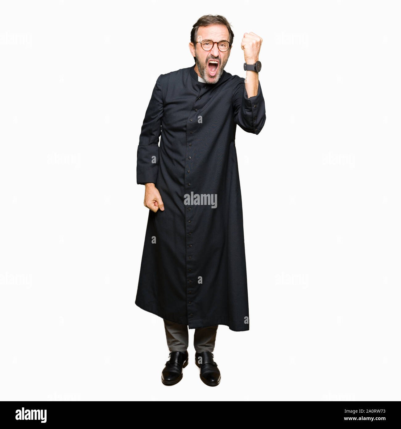 Middle age priest man wearing catholic robe angry and mad raising fist ...