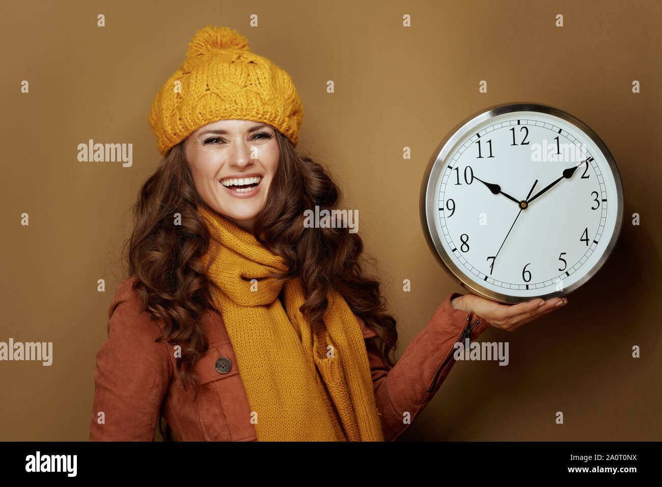 happy elegant woman in yellow beret and scarf showing round clock ...