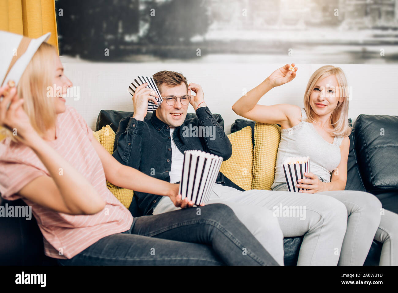 Three friends spending their weekend together sitting on sofa, eating ...