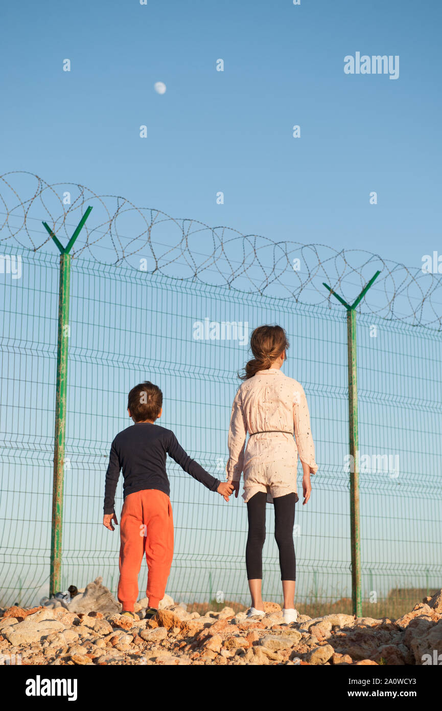 poor refugees kids on state border with high fence with barbed razor ...
