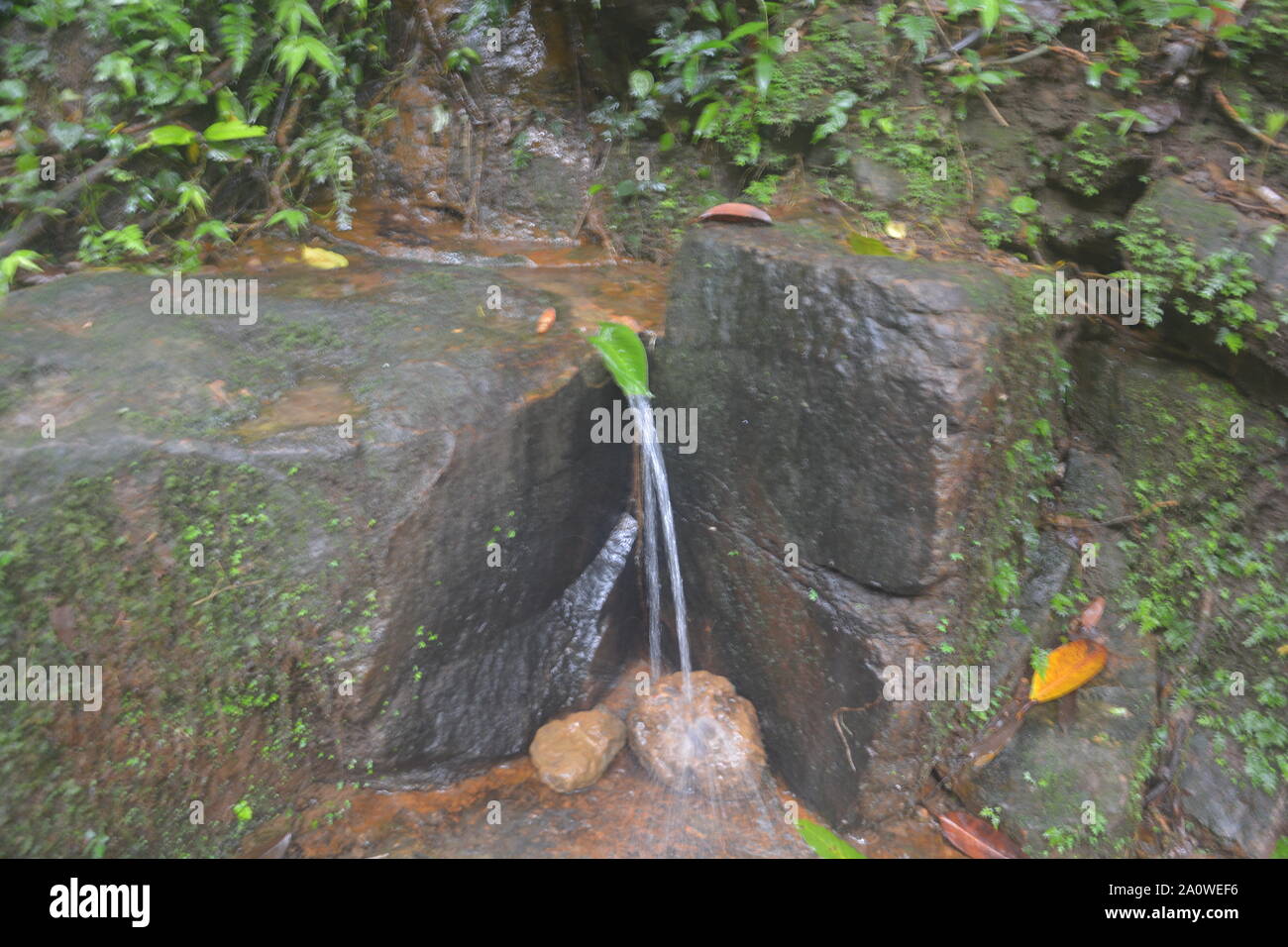 A small water fall or stream of water flowing between two big rocks in ...