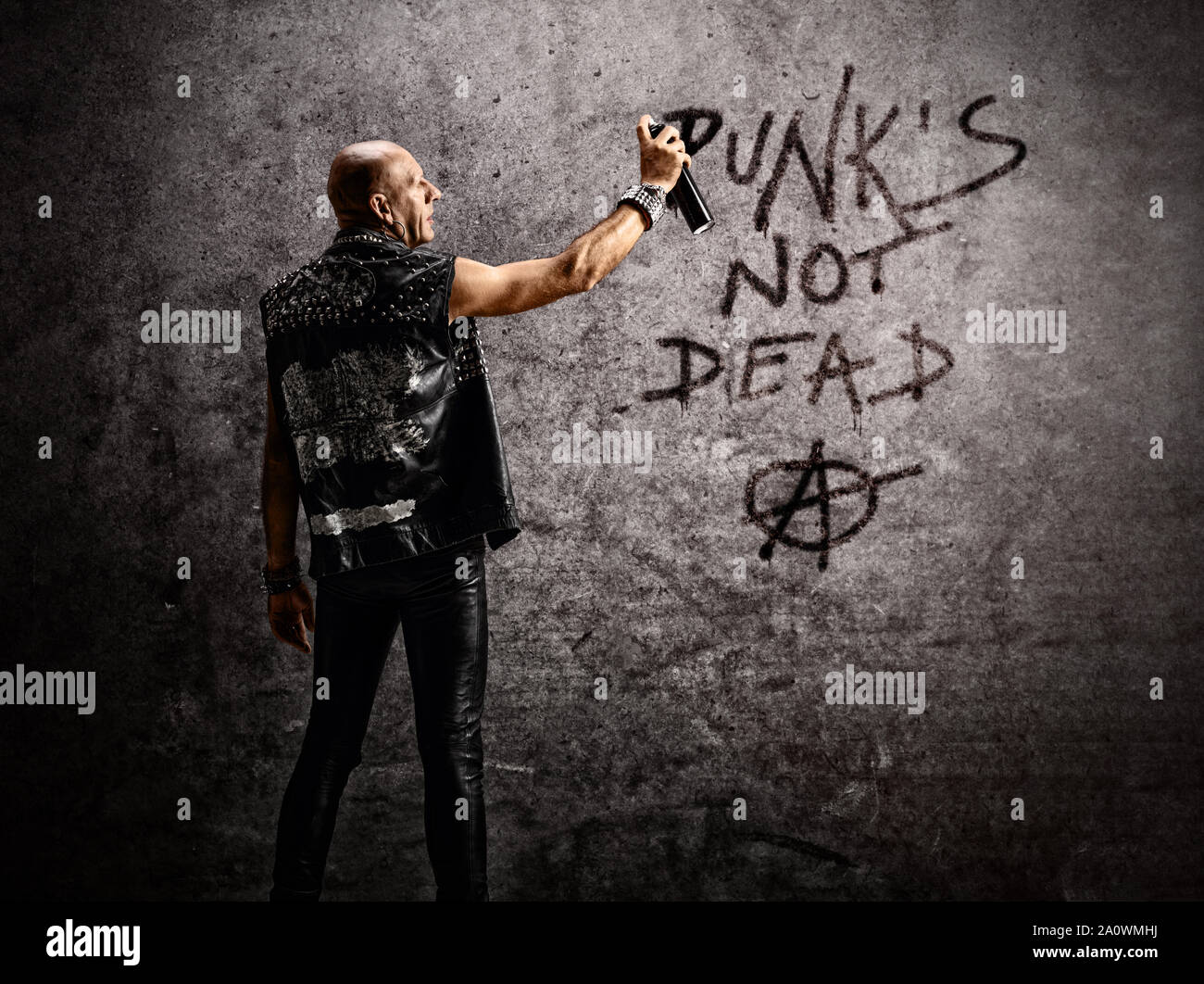 Punk in leather outfit writing a graffiti on a gray rusty wall saying ...