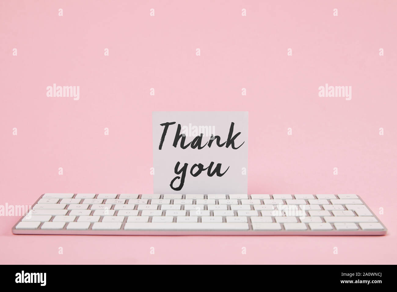 white card with thank you lettering near computer keyboard on pink ...