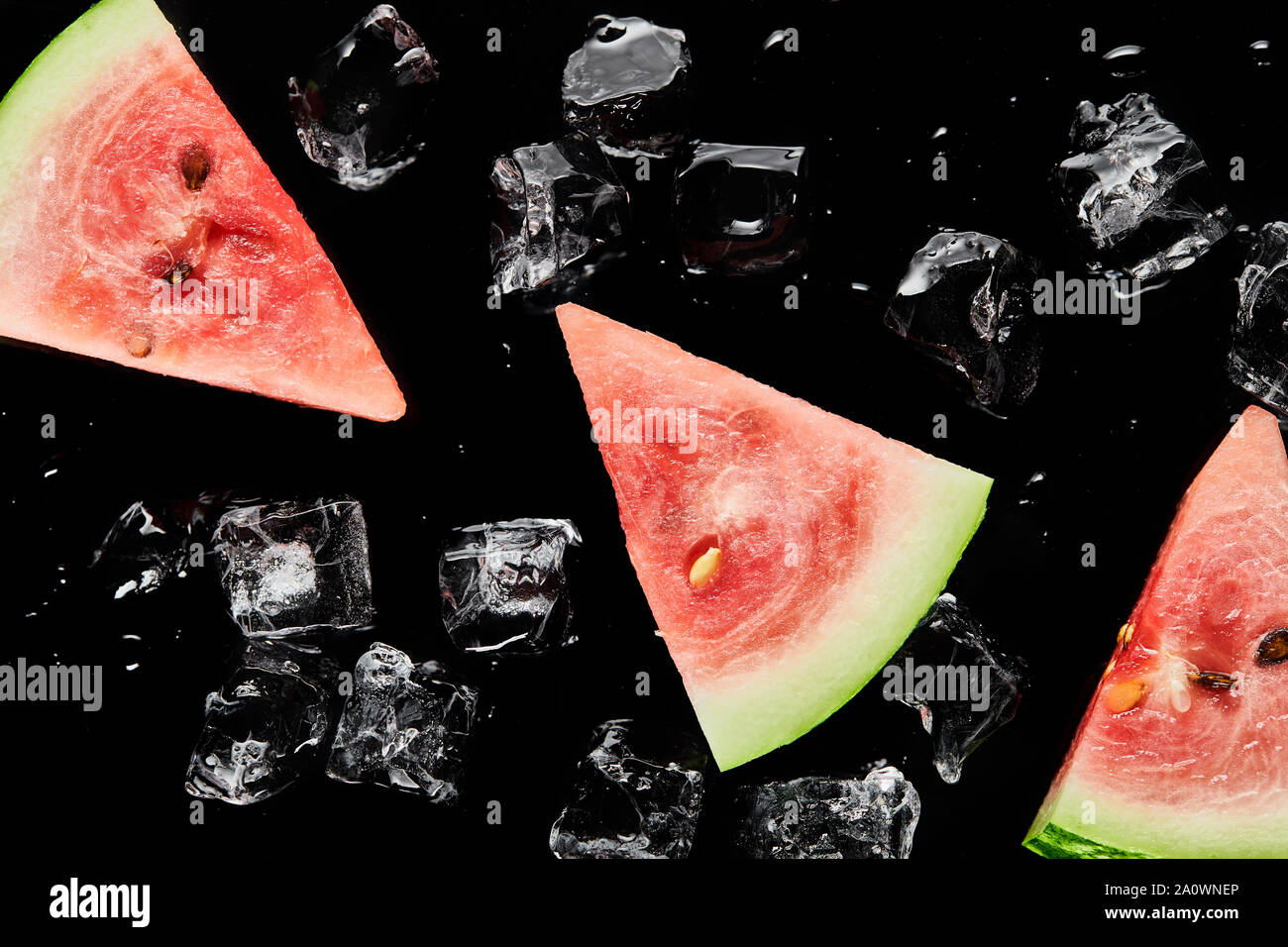 top view of red watermelon slices with melting ice isolated on black ...