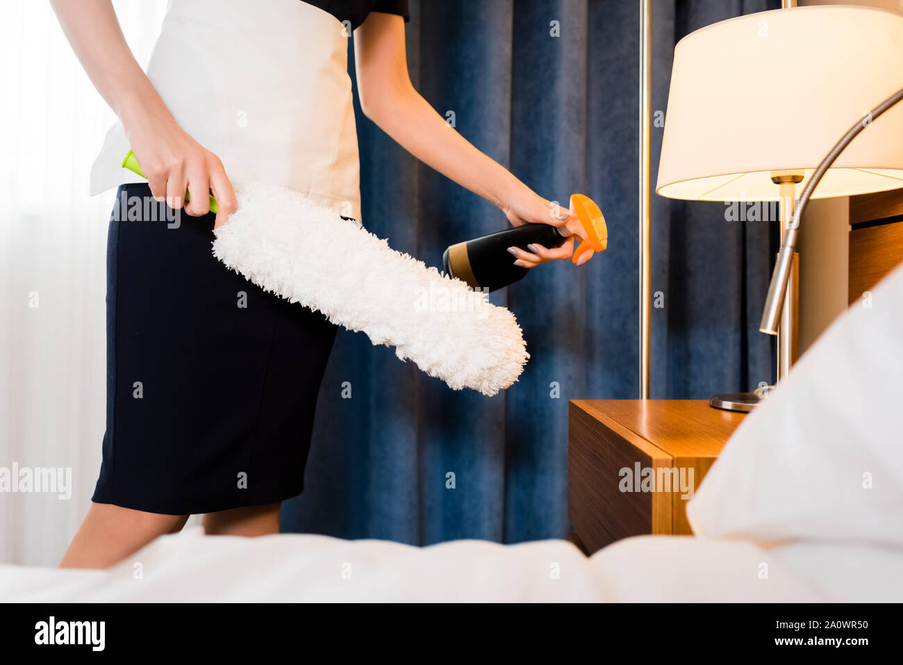 maid in uniform holding duster and bottle while cleaning hotel room ...