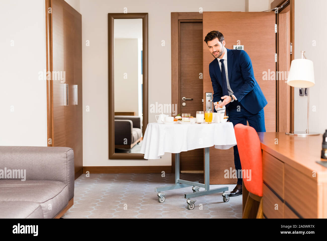 cheerful receptionist in formal wear gesturing near breakfast in hotel ...