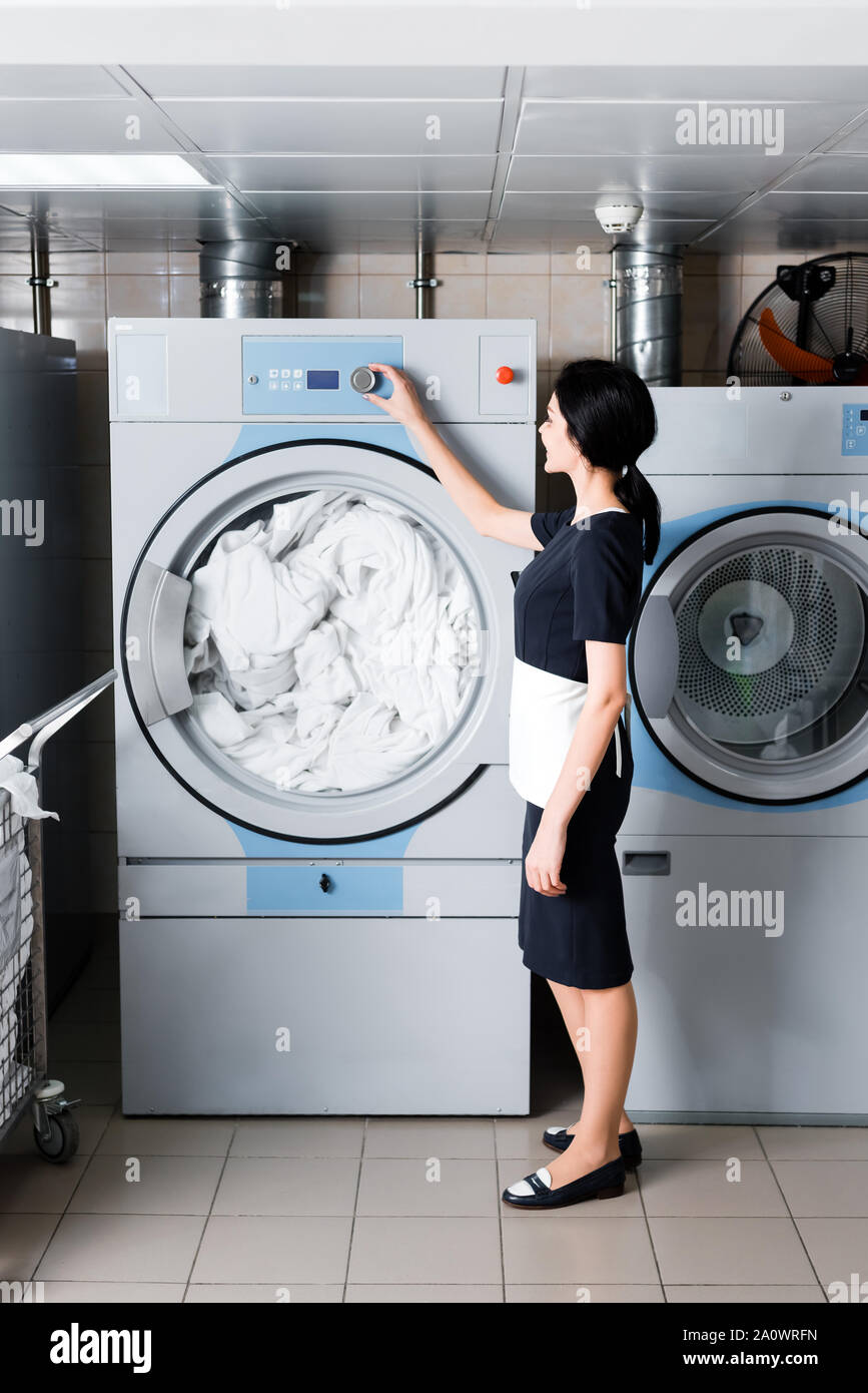 brunette maid standing and touching button on washing machine in ...