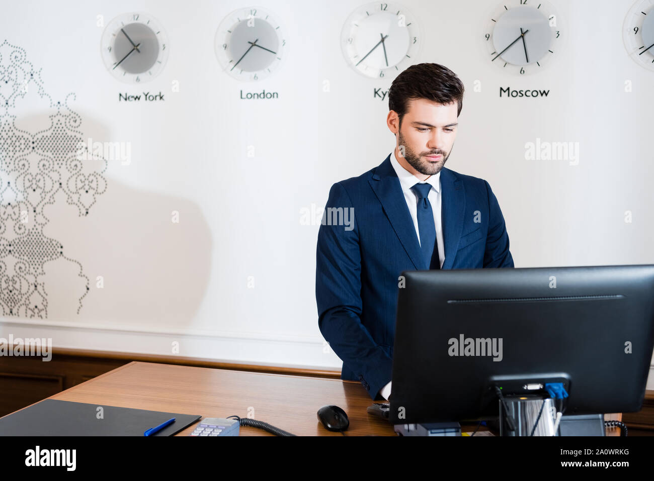 handsome receptionist in suit looking at computer monitor in hotel ...