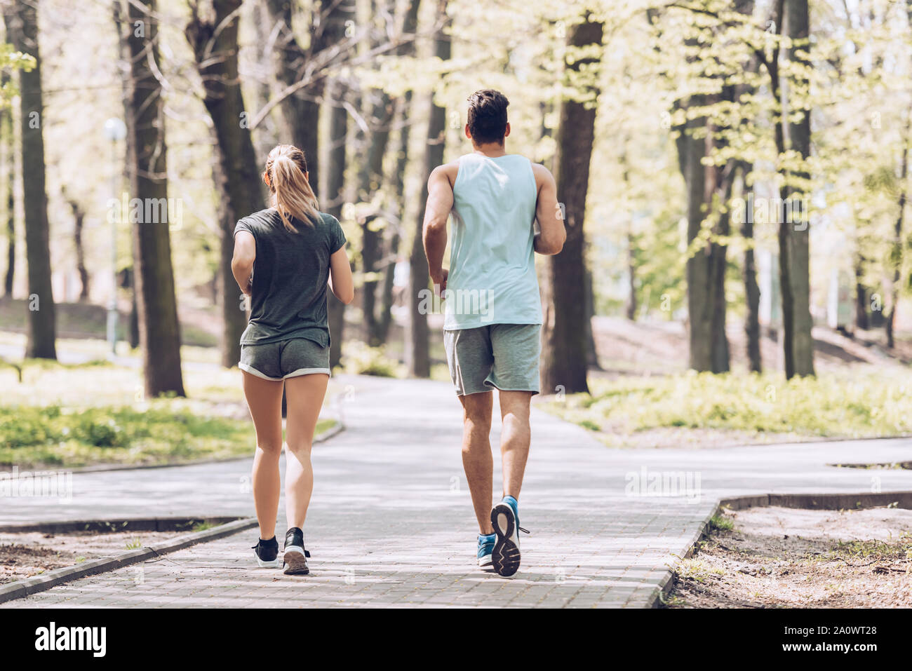 back view of young sportsman and sportswoman running on walkway in park ...