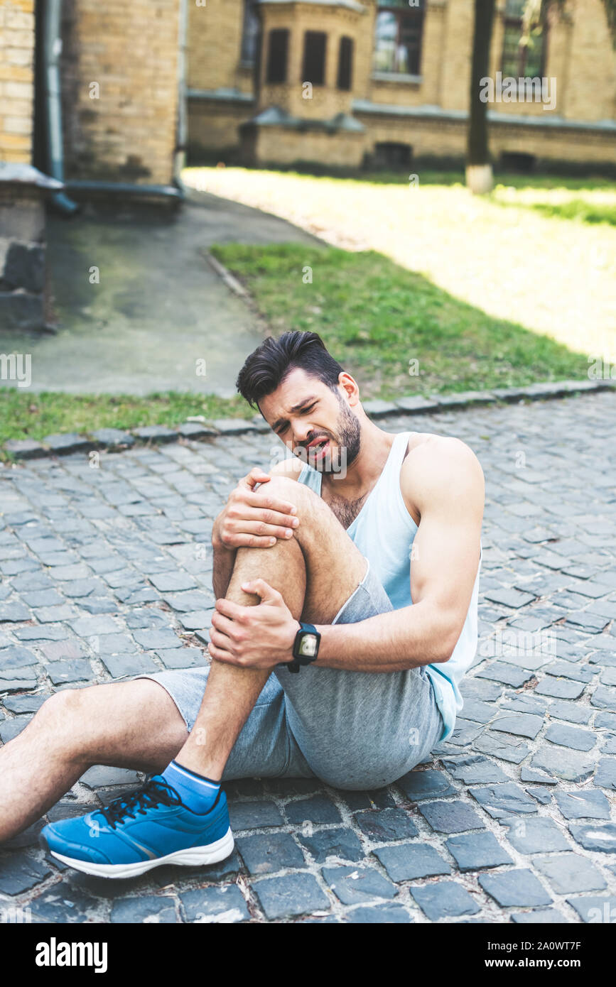 young sportsman suffering from pain while sitting on walkway and ...