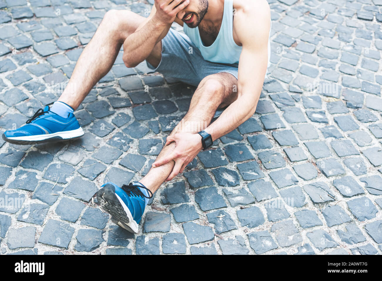 young sportsman suffering from pain while sitting on walkway, touching ...