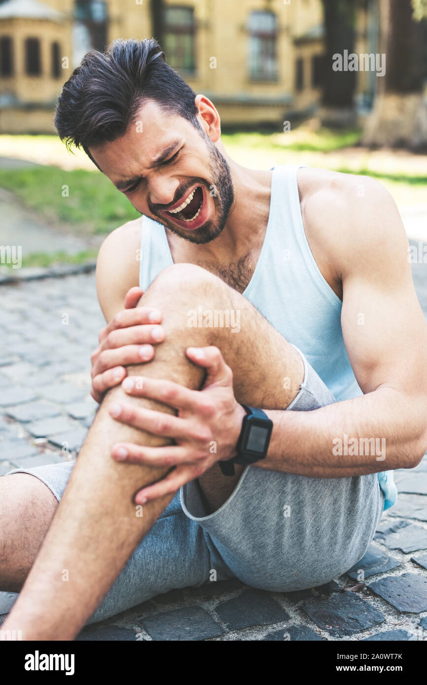 young sportsman suffering from pain and screaming while sitting on ...