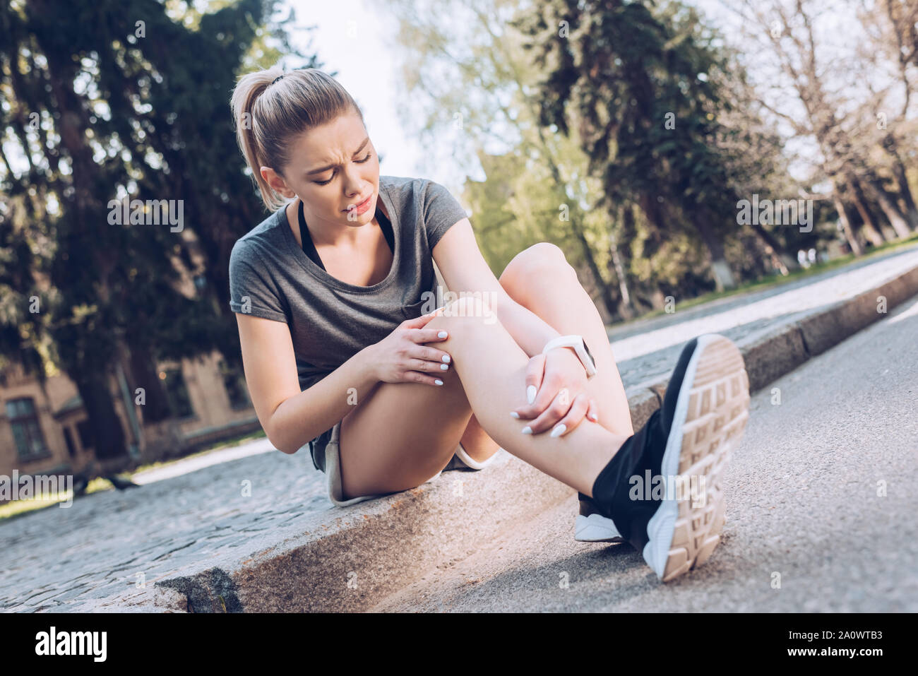 sad sportswoman suffering from pain while sitting on pavement and ...