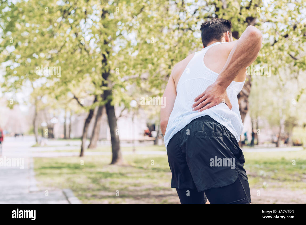 back view of sportsman suffering from pain while touching injured back ...