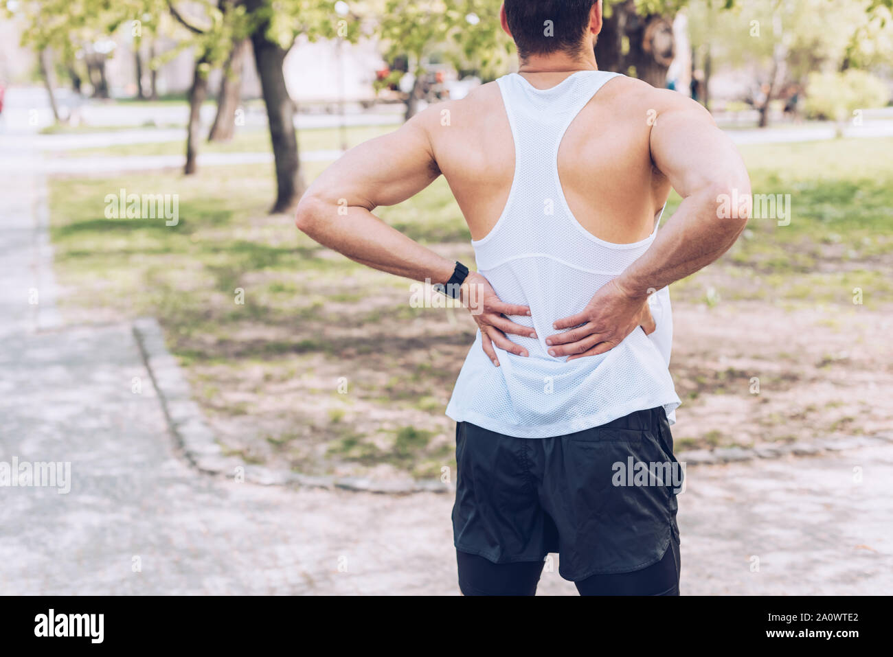 back view of young sportsman standing in park and touching injured back ...