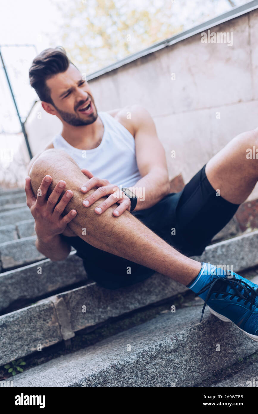 young sportsman sitting on stairs and suffering from pain while ...