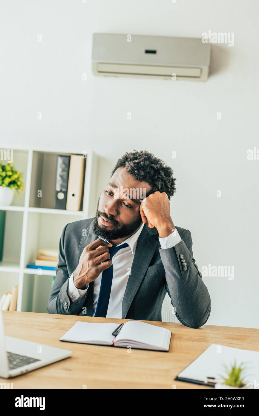exhausted african american businessman sitting at workplace under air ...