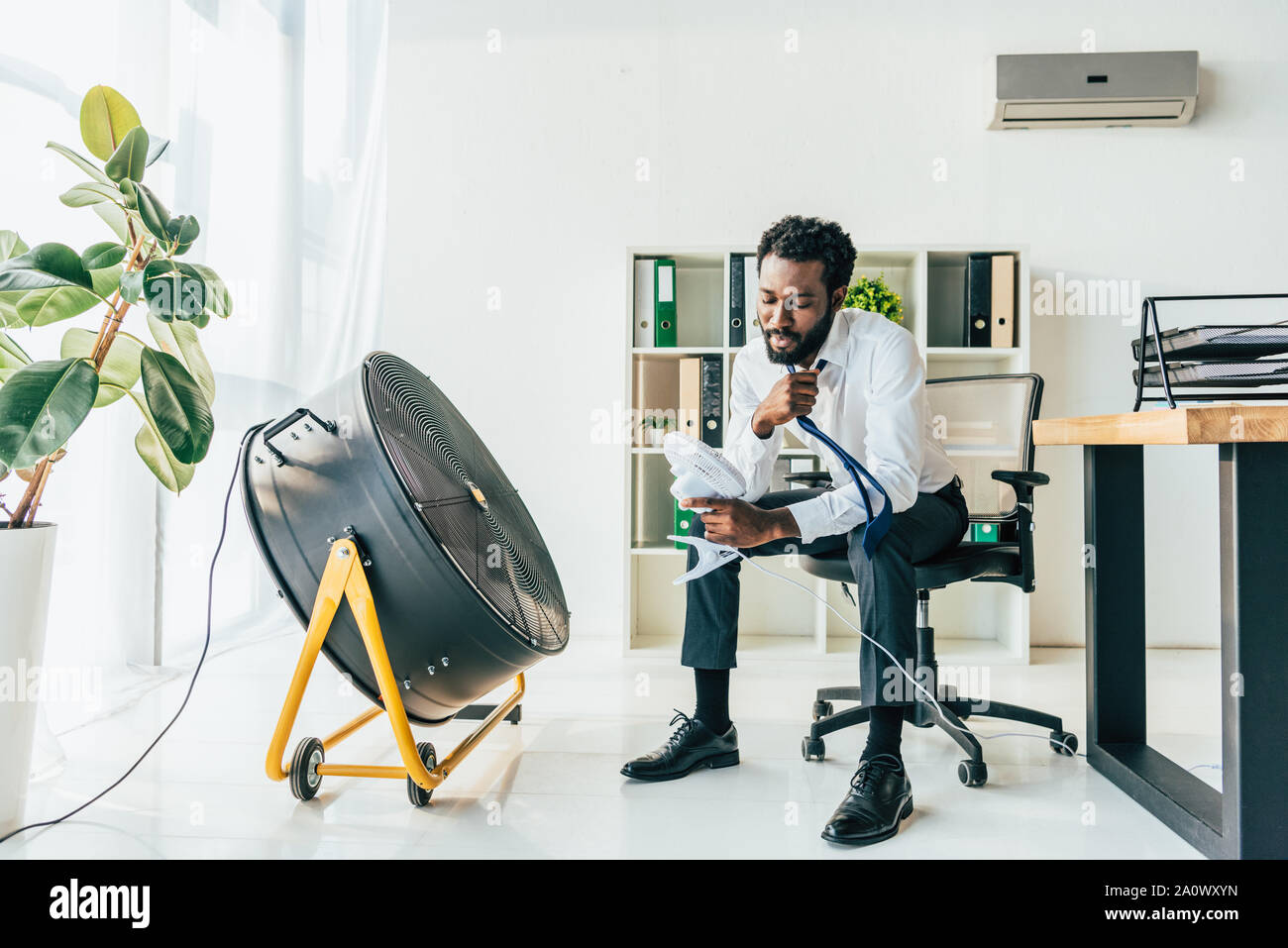 african american businessman holding desk fan while sitting in front of ...
