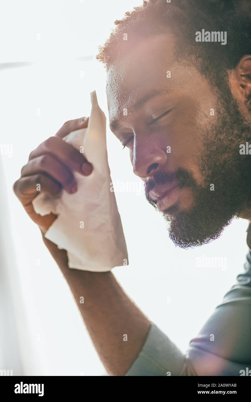 exhausted african american man holding napkin while suffering from ...
