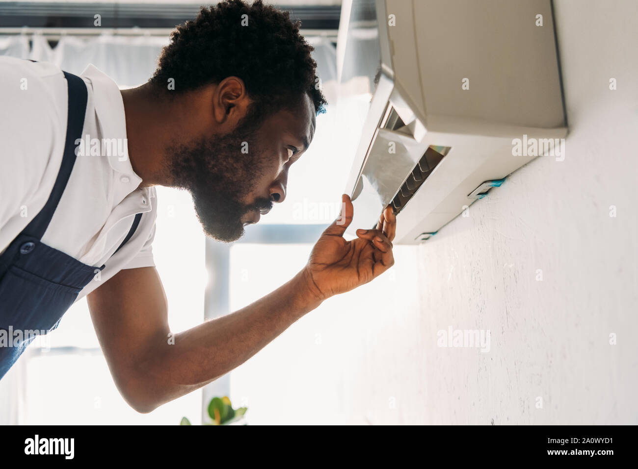 concentrated african american repairman looking at broken air ...