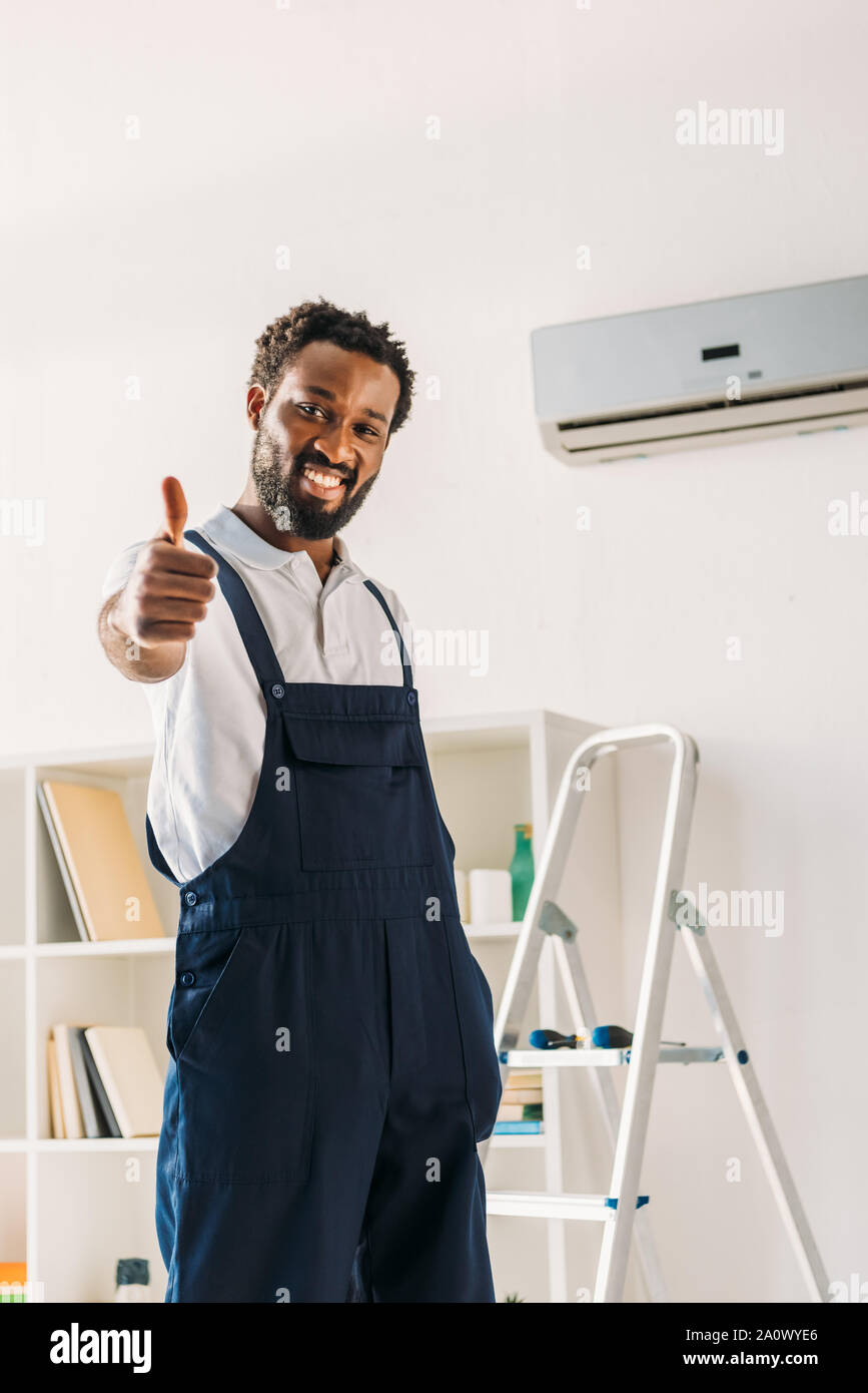 happy african american repairman standing on ladder under air ...