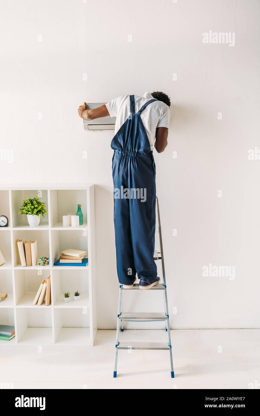 back view of african american repairman standing on ladder and fixing ...