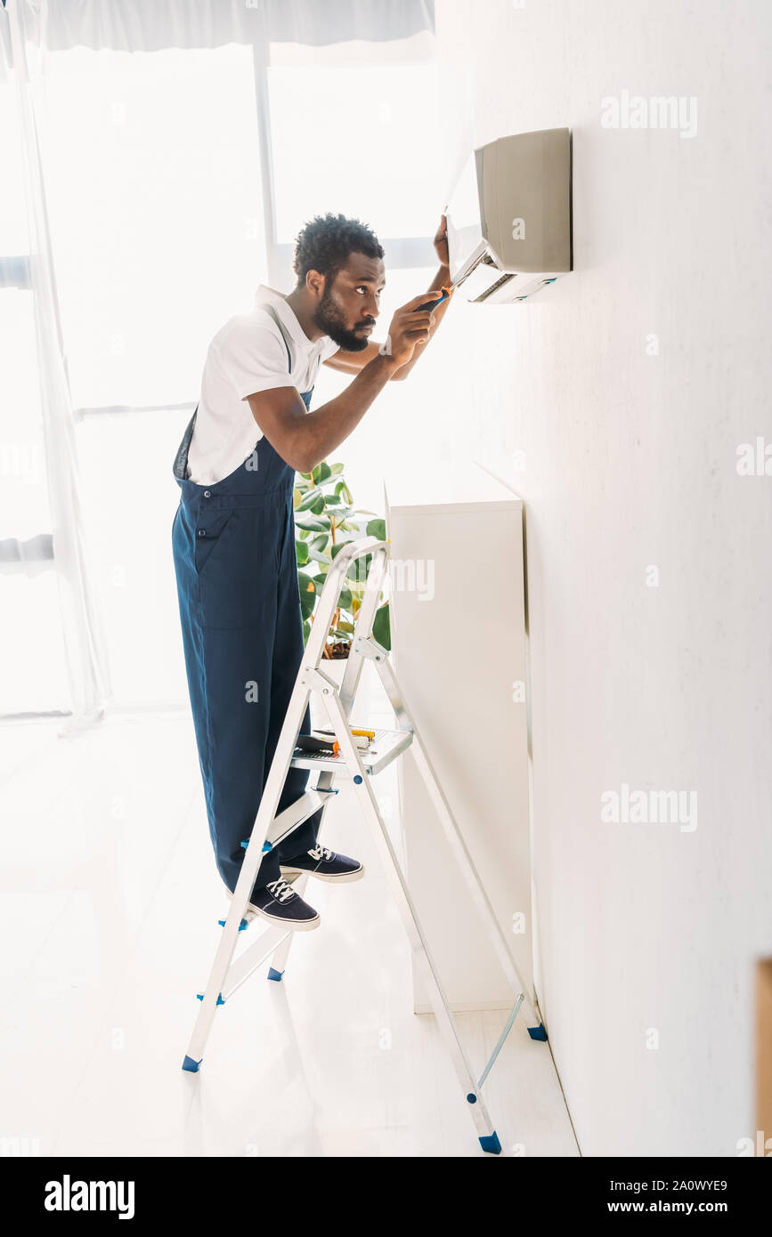 back view of african american repairman standing on ladder and fixing ...