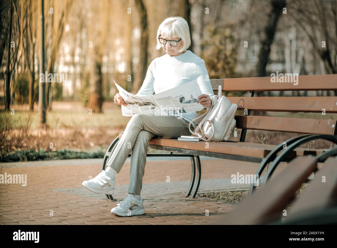 Serious superannuated madam wearing glasses and looking through paper ...