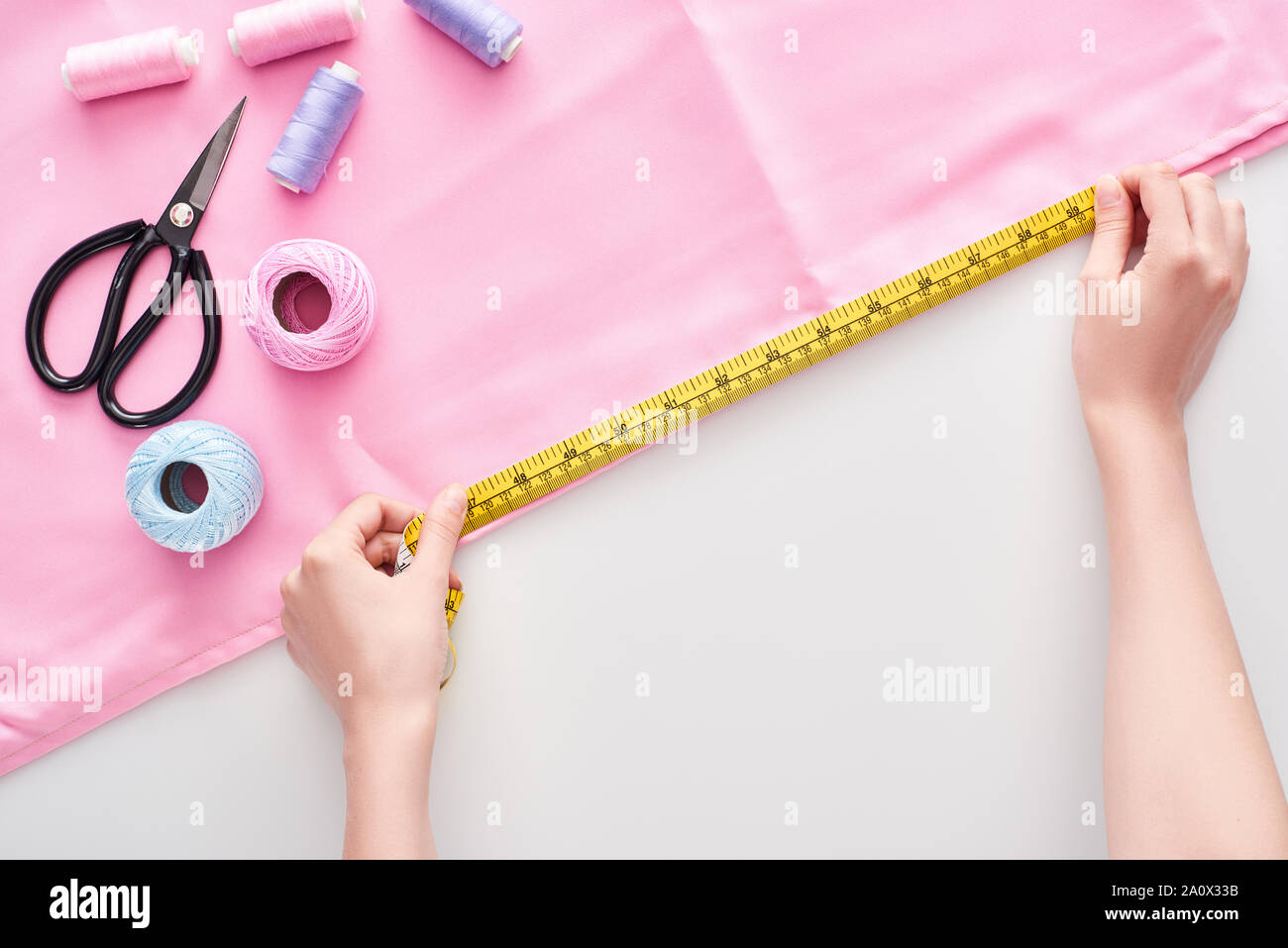 cropped view of seamstress measuring fabric with measuring tape on ...