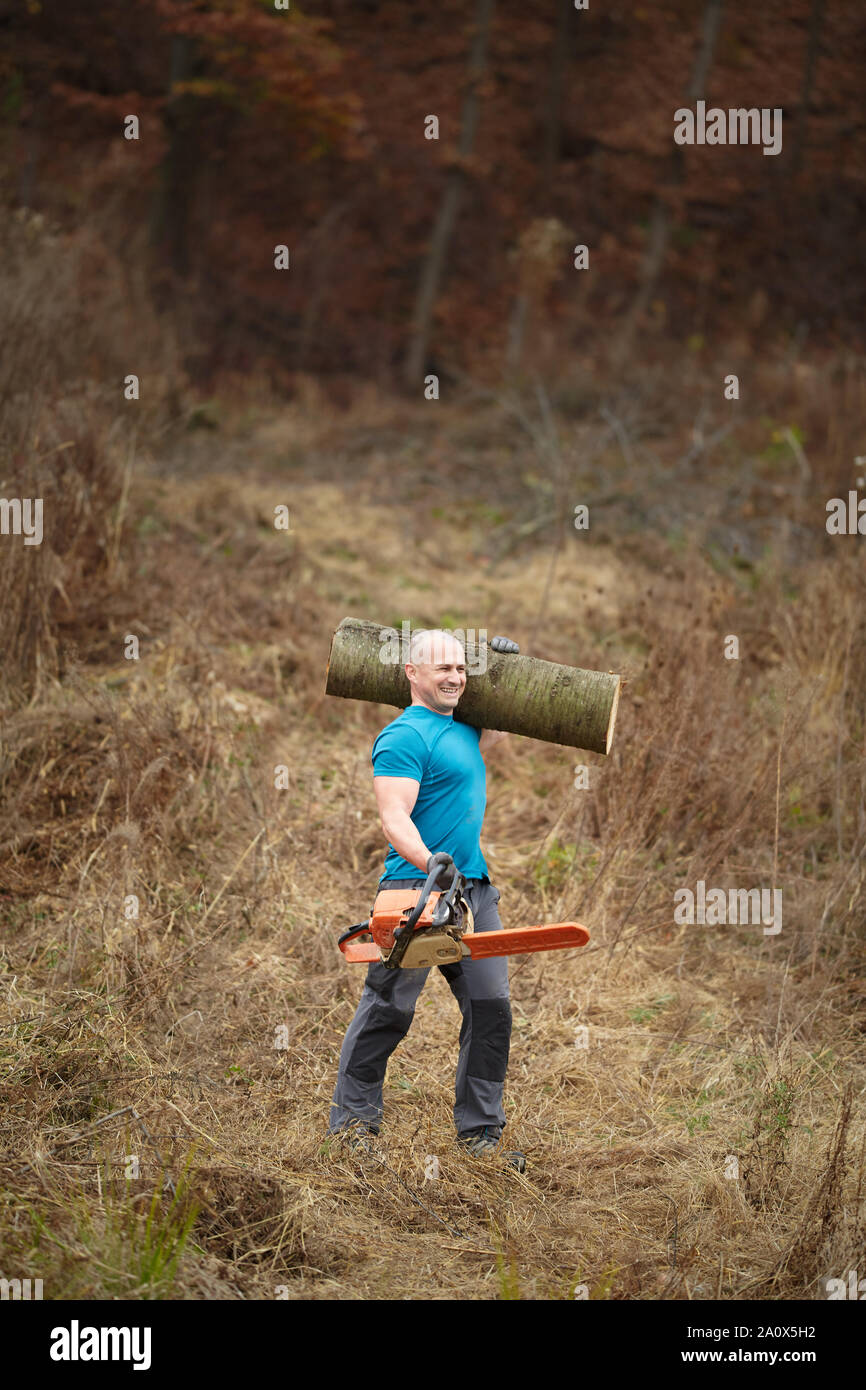 Strong muscular lumberjack with chainsaw, carrying a huge log on his ...