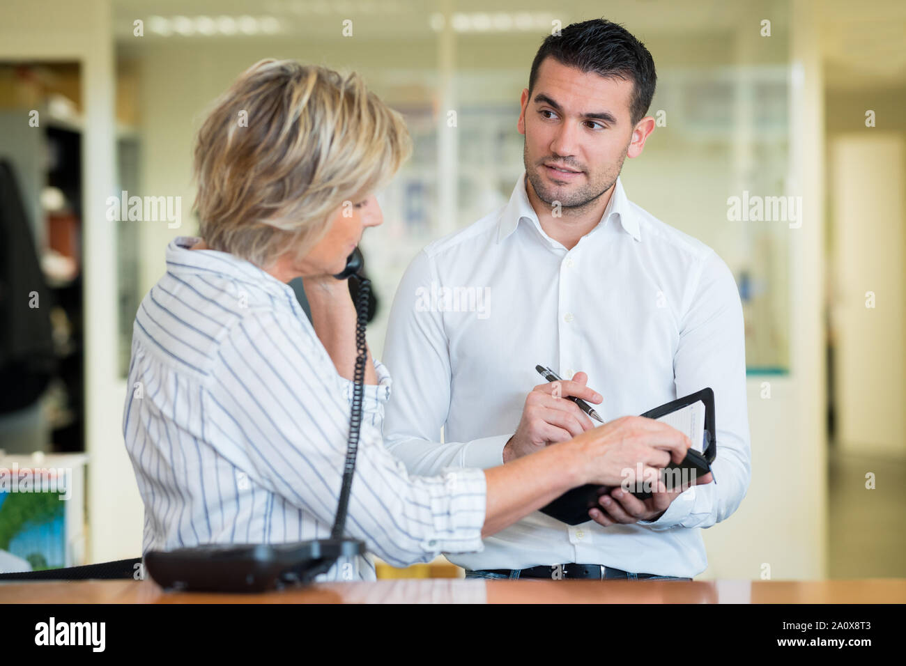 mature receptionist in discussion with man holding diary Stock Photo ...