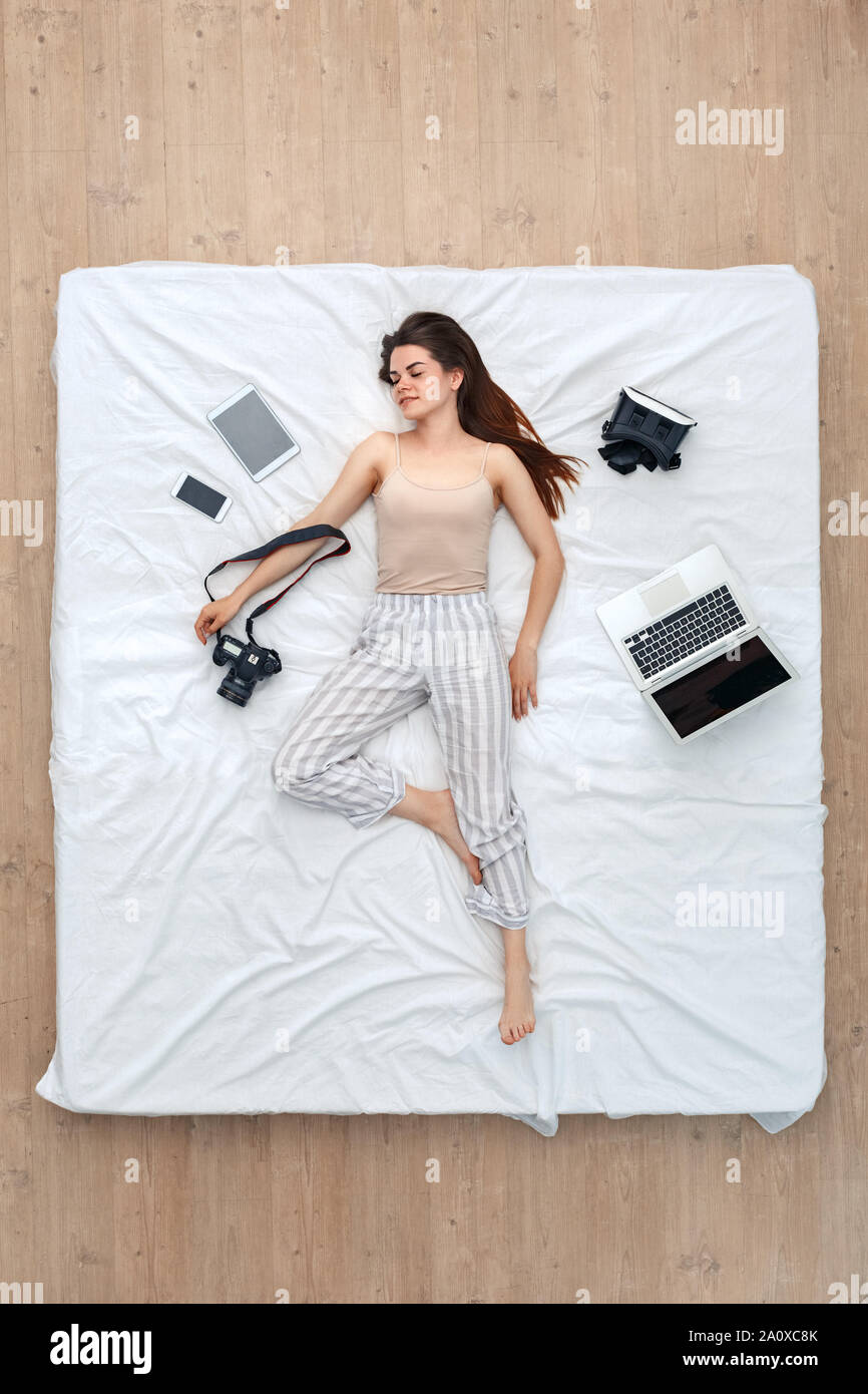 Bedtime. Young girl sleeping on bed top view surrounded by digital ...