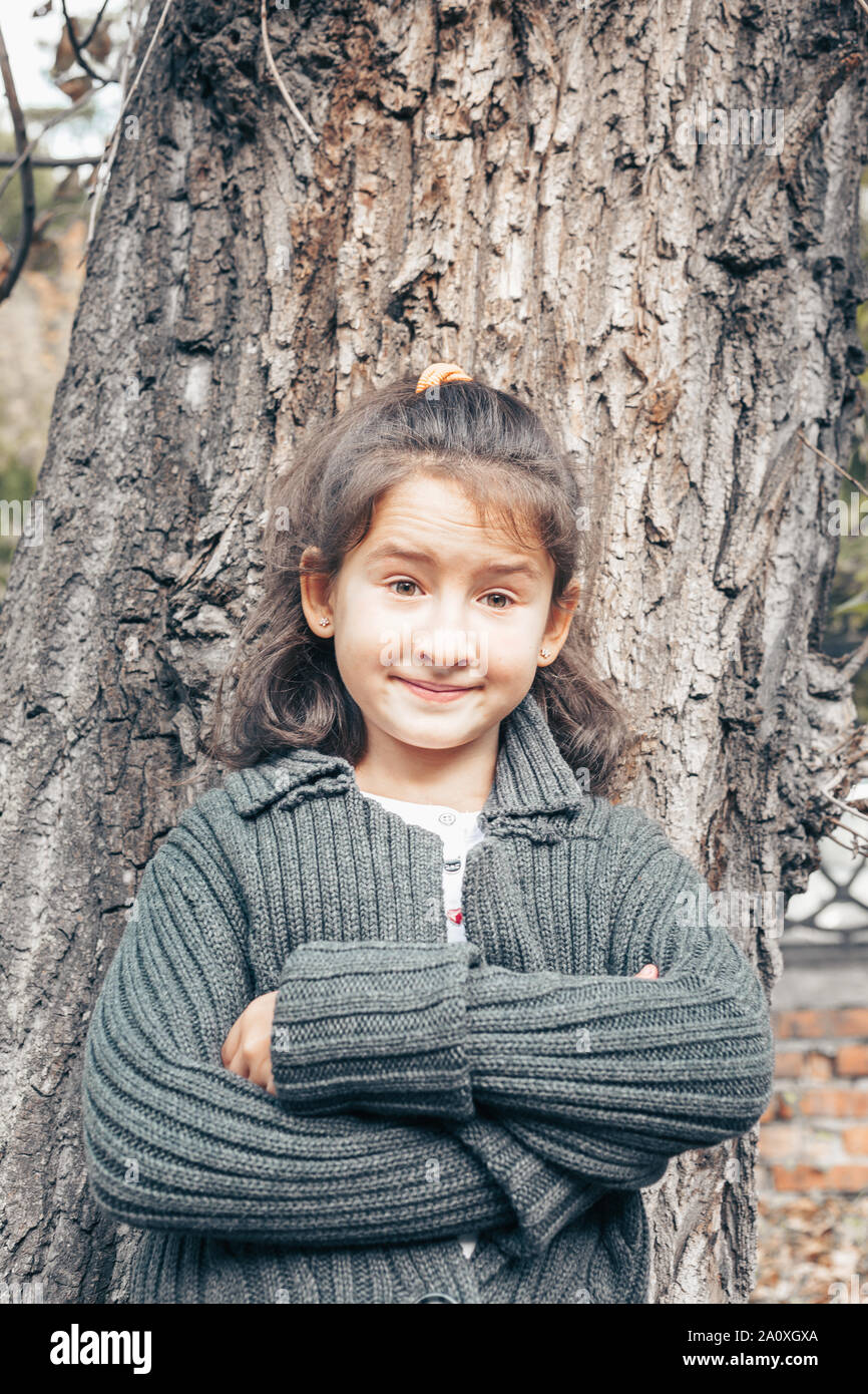 Cheerful cute girl. School age teenager girl stands near an old tree in ...
