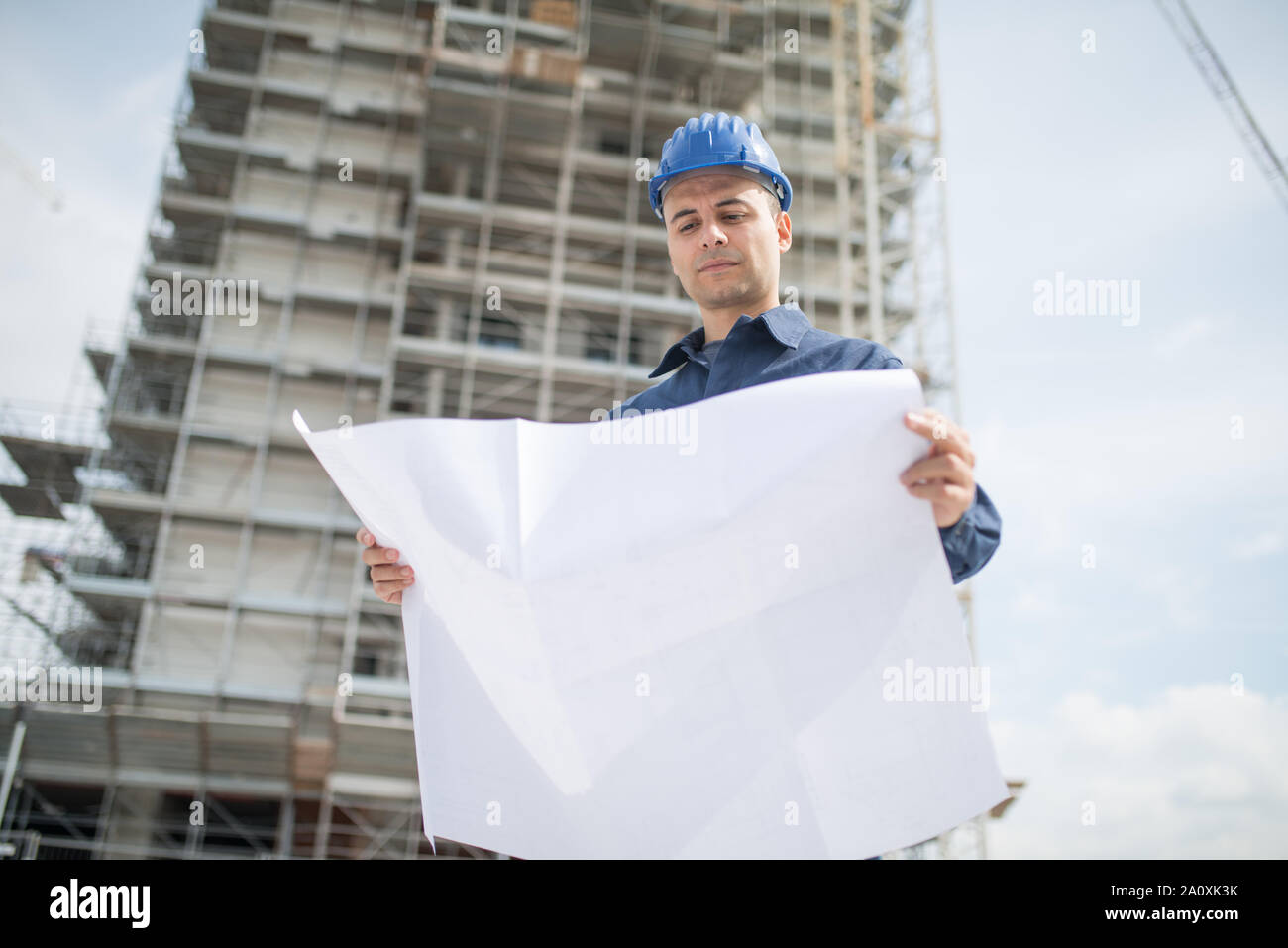 Smiling site manager reading a blueprint in front of a construction ...