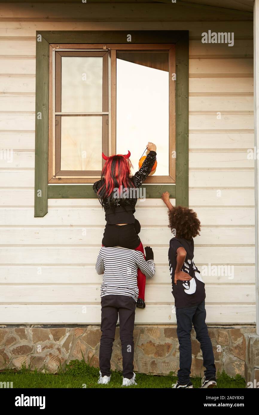 Back view of sneaky kids climbing window of house while trick or ...