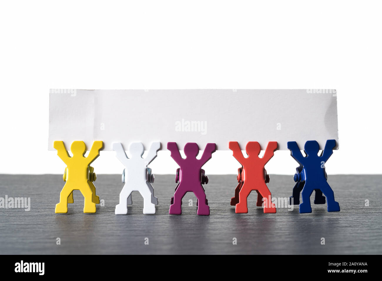 Colorful diverse miniature people figurines standing in a row on a dark ...