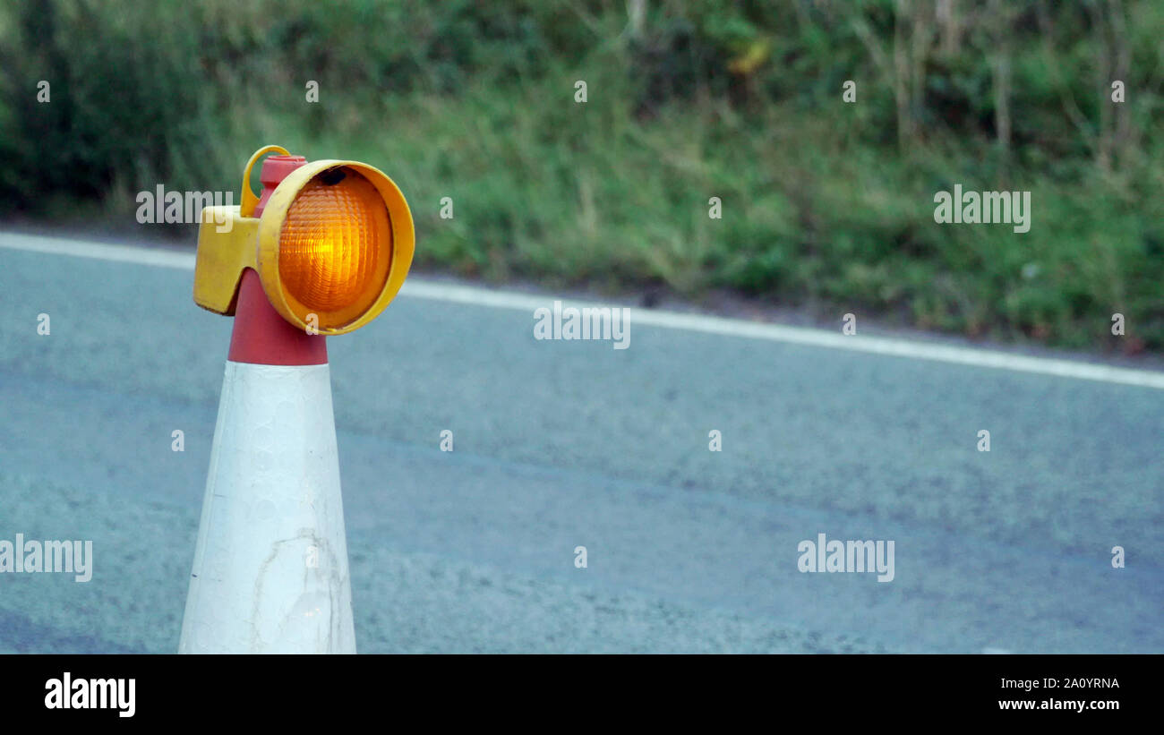 roadworks cone flashing on UK motorway at night with traffic passing ...
