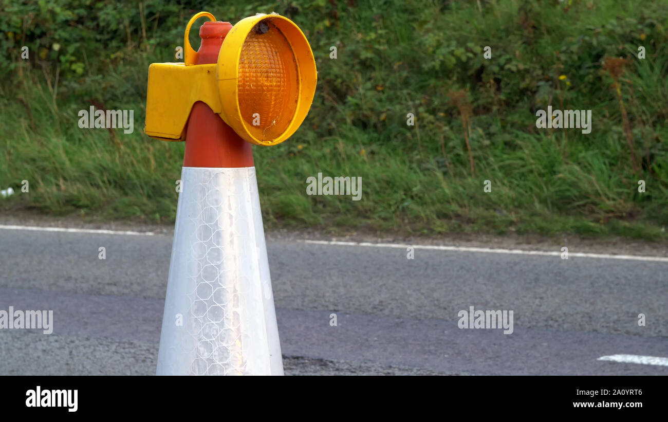 roadworks cone flashing on UK motorway at evening with traffic passing ...