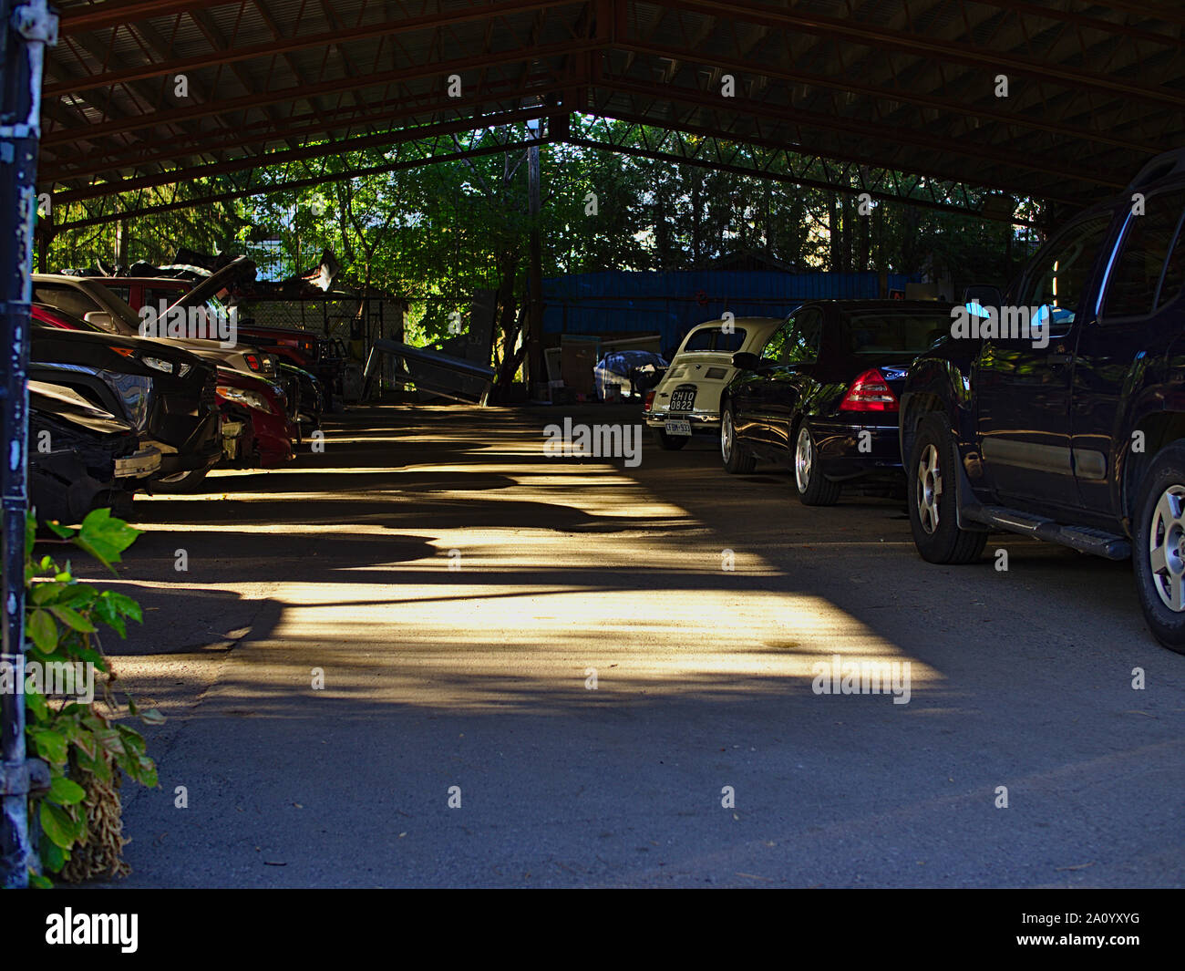 Sun and shadows inside a car repair shop, with lots of parked, broken ...